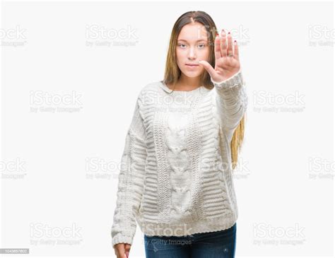 젊은 아름 다운 백인 여자는 손의 종 려를 가진 정지 노래를 하 고 격리 된 배경 위에 겨울 스웨터를 입고 얼굴에 부정적이 고 심각한 제스처와 경고 식입니다 갈색 머리에