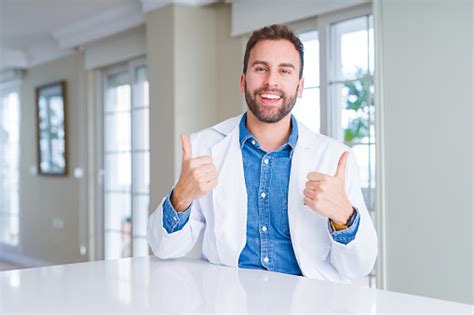 병원에서 의료 코트를 입고 잘 생긴 의사 남자 는 손과 긍정적 인 제스처를하고 성공 표지판 엄지 손가락미소와 행복 쾌활한