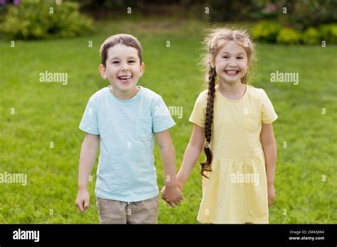 Cheerful Brother And Sister Holding Hands Standing In Garden Stock