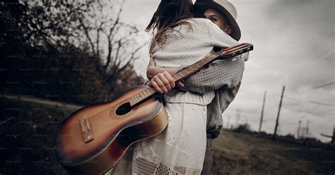 바람이 부는 들판에서 그의 보헤미안 집시 여자와 함께 기타 춤을 추는 남자 세련된 힙스터 커플 포옹 분위기 있는 관능적인 순간 세련된 모습소박한 결혼식 개념 사진