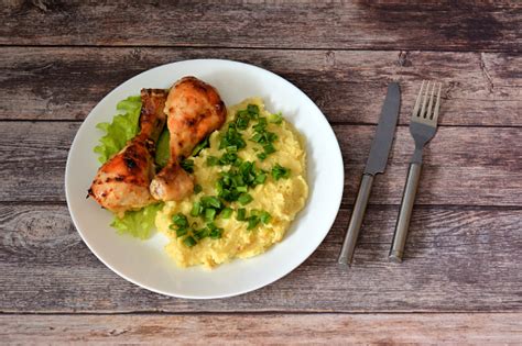 나무 테이블에 파와 구운 닭 다리 두 개를 곁들인 으깬 감자 한 접시 포크와 나이프 옆 0명에 대한 스톡 사진 및 기타 이미지 0명 감자 요리 구운 치킨 Istock