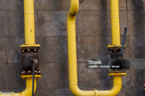 노란색 가스 파이프라인은 풍화된 회색 벽을 따라 달리며 현대 엔지니어링과 산업 미학의 조화를 드러냅니다 밸브는 에너지 시스템의 복잡한 설계를 반영하는 연결을 생성합니다 0