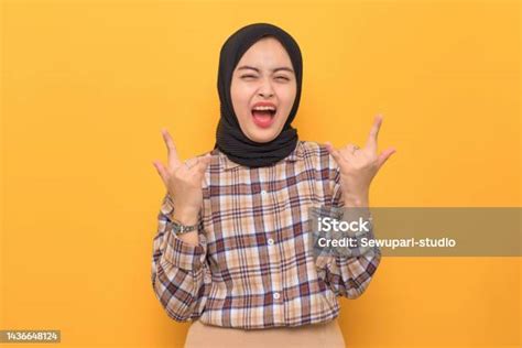 격자 무늬 셔츠를 입은 흥분한 젊은 아시아 여성이 노란색 배경에 고립 된 록 기호를하는 미친 표정으로 외치고 있다 20 24세에 대한 스톡 사진 및 기타 이미지 Istock