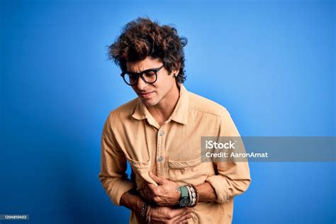 편안한 옷을 입은 젊은 잘생긴 남자는 메스꺼움 고통스러운 질병이 좋지 않아 위장에 손을 얹고 고립 된 파란색 배경 위에 서 있습니다 아쉬 컨셉 남자에 대한 스톡 사진 및