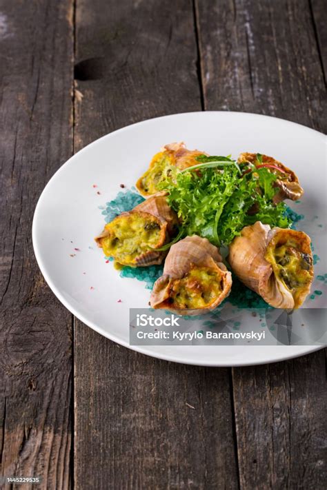 오븐에서 치즈와 타임으로 구운 라파나 그 옆에는 레몬 한 조각과 샐러드가 섞여 있습니다 음식은 흰색의 둥근 접시에 있습니다 파란색 굵은 소금이 접시에 흩어져 있습니다 접시는