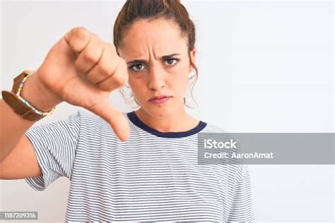 화가 난 얼굴로 고립 된 배경 위에 빵을 입고 있는 젊은 빨간 머리 현대 여성 엄지 손가락으로 싫어하는 것을 보여주는 부정적인