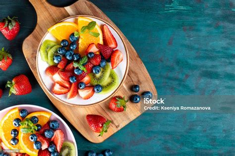 다양한 과일과 열매의 신선한 여름 샐러드 파란색 나무 소박한 배경 상단보기에 민트로 장식 된 접시에 키위 오렌지 딸기와 블루 베리 텍스트 공간을 복사 감귤류 과일에 대한