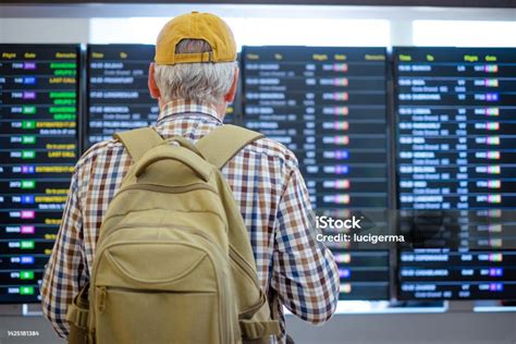 공항의 노인이 수하물 카트를 밀고 시간표 일정을보고 항공편 출발을 확인합니다 배낭과 여행 가방을 가진 여행자 개념 사람들 공항에