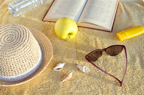 밀 짚 모자 조개 썬 탠 크림 선글라스 사과 병에 물이 들어가 베이 지 비치 타월에 책을 열었습니다 부드러운 저녁 햇빛 읽기에