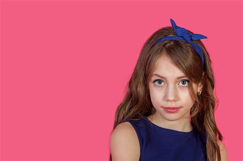 분홍색 고립된 배경에서 포즈를 취하는 파란 옷을 입은 완벽한 작은 표지 소녀의 얼굴 카메라를 보는 지루함 슬픈 감정의 아이