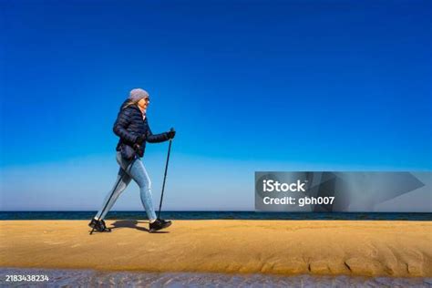 진한 파란색 재킷 청바지 및 겨울 모자를 입고 아름 다운 젊은 여자가 겨울에 화창한 날에 모래 해변을 걷는 북유럽 훈련 앞 View 봄에 대한 스톡 사진 및 기타 이미지