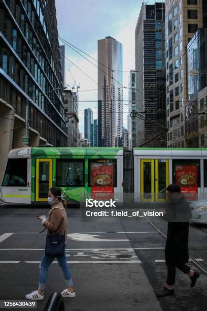 사설 코로나 바이러스 전염병 두 번째 파도로 인해 3 단계 제한 동안 일반적으로 바쁜 멜버른의 중심에있는 도시 거리를 횡단하는 얼굴 마스크와 휴대 전화에 남자를 입고 있는