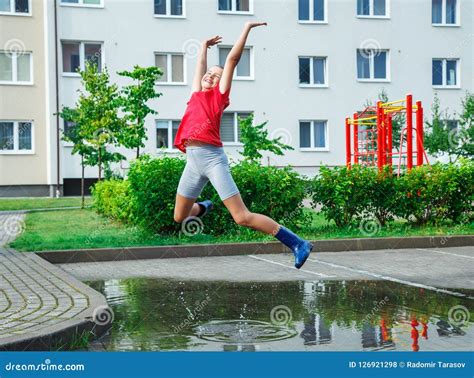 Девушка в голубых резиновых ботинках скача в лужицу после дождя Стоковое Фото изображение