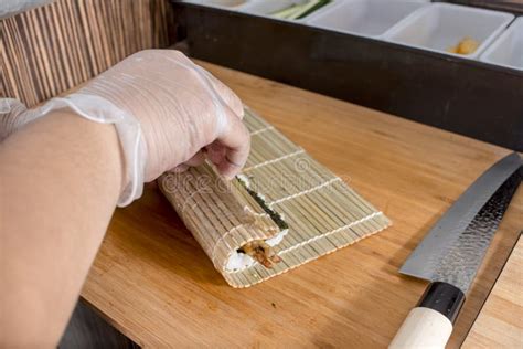 Using A Makisu To Roll A Batch Of Tempura Maki Wearing Plastic Gloves