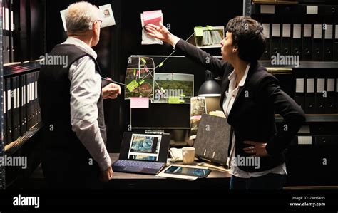 Two Officers Examine Classified Records In Incident Room Reading Witness Statements To Create