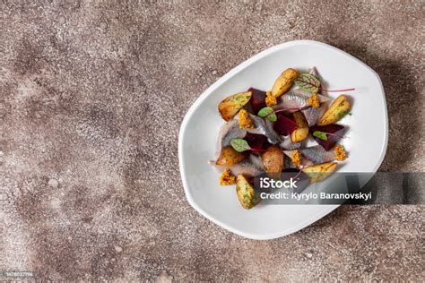 구운 감자 웨지 비트 뿌리 청어 및 양상추 조각이 든 접시 음식은 타원형의 흰색 세라믹 접시에 놓여 있습니다 접시는 직물 배경 커피 색상에 서 있습니다 0명에 대한 스톡