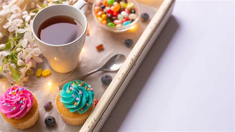 밝은 케이크 컵 케이크는 글을 위한 공간을 가진 흰색 배경에 꽃 지점과 빛나는 화 환이 있는 트레이에 커피 또는 차와 컬러 도트를 한 잔 모닝 무드 마실 것에 대한 스톡