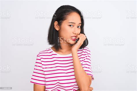 줄무늬 티셔츠를 입은 젊은 중국 여성은 손톱을 물고 손톱을 물고 손에 스트레스와 긴장 찾고 고립 된 흰색 배경 위에 서있다 불안
