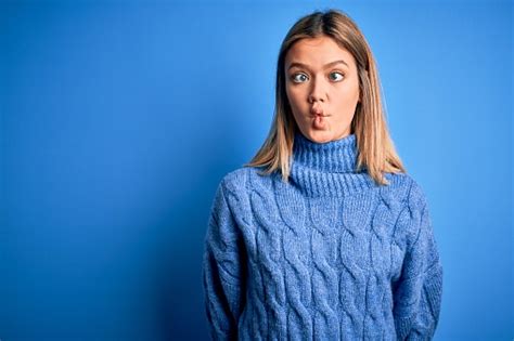 젊은 아름다운 금발 의 여자 겨울 울 스웨터 를 입고 푸른 고립 된 배경 에 입술 미친 코믹 제스처물고기 얼굴을 만들기 재미있는 표현 겨울에 대한 스톡 사진 및 기타 이미지