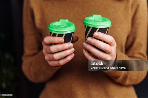 커피 한 잔과 손을 클로즈업 소녀는 테이크 아웃 커피를 샀다 아름다운 우유 거품을 곁들인 아름답고 향기롭고 갓 내린 카푸치노 녹색 스트립이 있는 블랙 컵 가루로 빻은에 대한