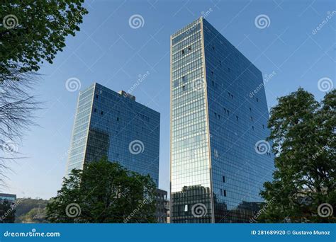 Low Angle Image Of Two Twin Rectangular Buildings With Glass Enclosures On Blue Sky With Trees