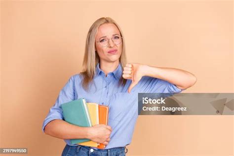 베이지색 배경에 다채로운 책을 들고 엄지 손가락 아래로 기호로 불만 제스처를 표시하는 표현적인 젊은 여성 30 34세에 대한 스톡 사진 및 기타 이미지 Istock