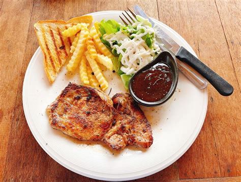 A White Plate Topped With Meat Fries And Coleslaw On Top Of A Wooden Table