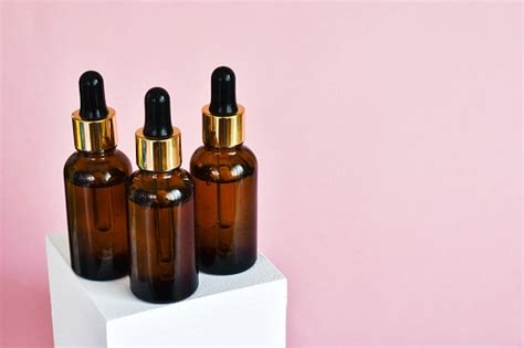 분홍색 배경에 흰색 연단에 파이펫이있는 갈색 유리 병에 천연 히알루론 세럼 복사 공간을 복사합니다 대체 의학 방향족 화장품 스킨