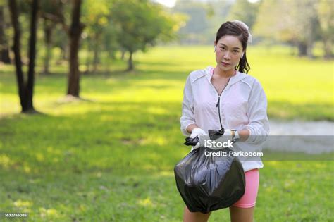 아침 달리기 후 젊은 아름다운 아시아 자원 봉사 여성은 쓰레기 봉투를 들고 공원 잔디밭에서 쓰레기를 줍고 자원 봉사 환경 청소