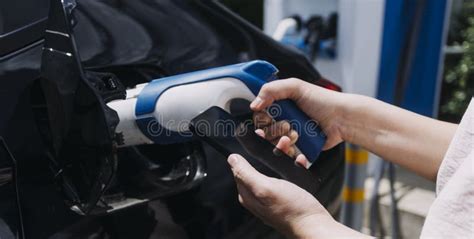 Hand Plugging In A Charger In An Electric Car Socket Electric Car Or Ev Is Charging At Station