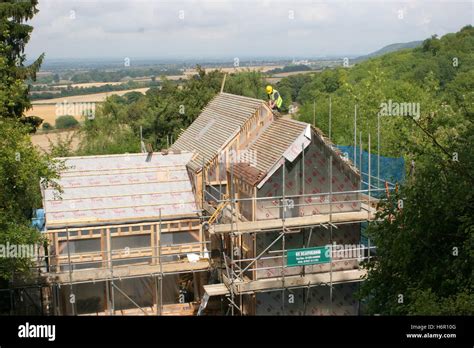 A Single Roofer Nails Timber Battens To The Roof Of A Timber House On An Oxfordshire Hillside