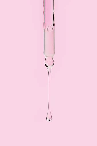 얼굴 혈청이 있는 유리 피펫과 밝은 분홍색 배경에 떨어지는 물방울 거품이 있는 액체 스킨 케어 화장품 근접 촬영 물방울에 레티놀이 함유 된 혈청 에센셜 오일 또는 젤 매크로