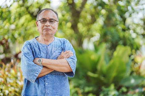 팔을 들고 서 있는 태국 노인이 흐릿한 자연 배경으로 카메라를 바라보며 교차했다 공간을 복사합니다 건강한 생활방식에 대한 스톡