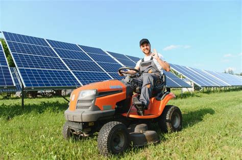 A Man Working At Solar Power Station A Worker On A Garden Tractor Mows