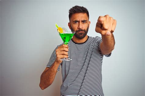 젊은 인도 남자 마시는 칵테일 과 술 위에 서 고립 된 흰색 배경 가리키는 손가락으로 카메라와 당신에 게 손 기호 앞에서 긍정적이 고 자신감 제스처 가리키기에 대한 스톡