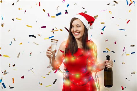 아름 다운 백인 웃는 젊은 행복 한 여자 빨간 드레스 크리스마스 모자와 손전등 유리와 흰색 바탕에 샴페인의 병을 화 환에 산타