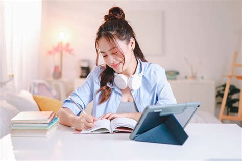 노트북을 사용하여 책상에 앉아 웹 세미나 온라인 학습 교육 과정 학습 회의 전자 학습 개념을 보면서 메모를하는 미소 짓는 아시아 여성 가상현실에 대한 스톡 사진 및 기타