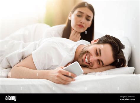 Wife Spying While Cheating Husband Texting On Cellphone In Bedroom