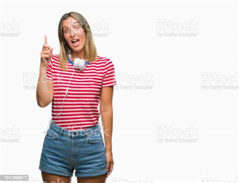 아름 다운 젊은 여 자가 듣기 음악 성공적인 아이디어를 고립 된 배경 가리키는 손가락에 헤드폰을 입고 종료 하 고 행복 번호 하나입니다 가리키기에 대한 스톡 사진 및 기타