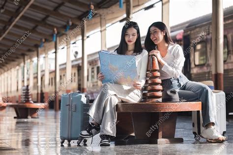 Young Lesbian Couple Waiting For Train At Station With Luggage Reading