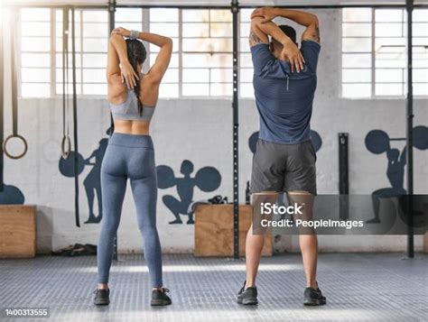 뒤에서 활동하는 두 명의 백인 운동 선수가 체육관에서 운동하는 동안 팔꿈치를 머리 뒤의 척추쪽으로 손으로 당겨 팔과 삼두근을 스트레칭합니다 피트니스 센터에서 운동 훈련을