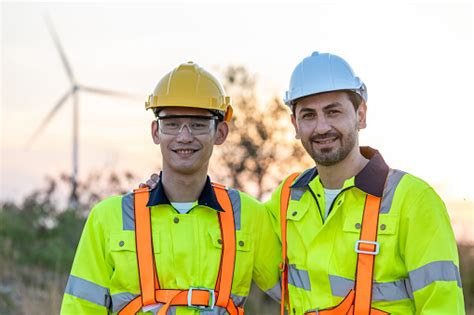 풍력 터빈 현장에 서 있는 두 남성 기술자의 초상화 풍차 농장에서 환경 청정 에너지를 개발하기 위해 안전 장비를 착용하고 카메라를 바라보는 혁신 엔지니어 남성 2명에 대한
