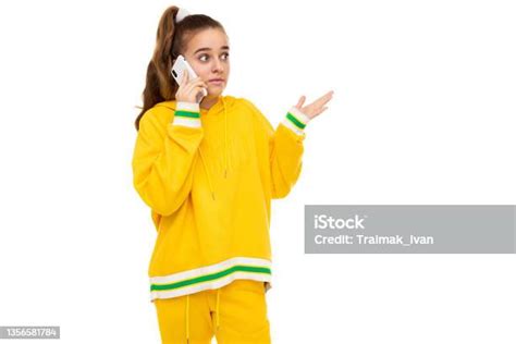 텍스트 에 대한 여유 공간이있는 흰색 배경에 고립 된 휴대 전화에서 이야기 녹색 줄무늬와 세련된 노란색 트랙 수트에 포니 테일과 어두운 머리와 아름다운 충격과 놀란 소녀의