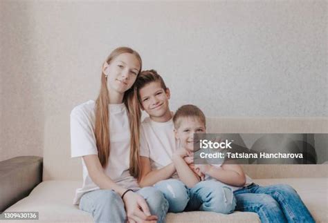 흰색 티셔츠와 청바지를 입은 세 명의 어린이와 두 명의 소년이 집 소파에 앉아 미소를 짓고 있습니다 형제 자매에 대한 스톡 사진 및 기타 이미지 Istock