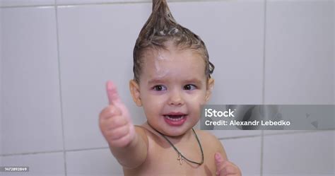 화장실에 있는 어린 소녀는 엄지손가락을 치켜세웁니다 어린 소녀는 샴푸로 머리를 씻는 것을 좋아합니다 귀여운 아기가 목욕에