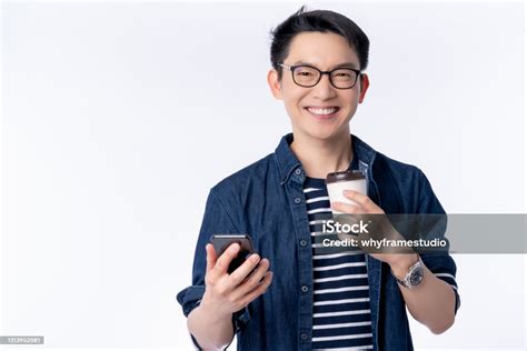 스마트 매력적인 아시아 안경 남성 손 잡고 뜨거운 음료 커피 손 검색 및 신선함과 즐거운 캐주얼 드레스 화이트 배경으로 스마트 폰 화면을 보고 검색에 대한 스톡 사진 및