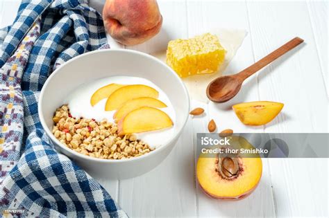 흰색 나무 배경에 숟가락 벌집 복숭아와 함께 구성에 흰색 그릇에 저지방 요구르트와 흰색 밀 그래놀라 건강한 아침 식사 음식 아침 식사 만들기 글루텐 프리 0명에 대한 스톡