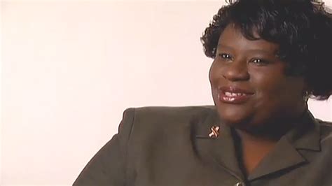A Woman Wearing A Suit Jacket Being Interviewed Against A White Background