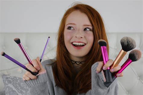 다른 크기의 메이크업 브러쉬의 선택을 들고 긴 생강 빨간 머리와 미소 십대 소녀의 이미지 창백한 피부와 주근깨 파운데이션과 파우더 브러시 브론저 컨실러 블러셔 얼굴 윤곽