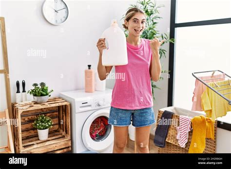 Young Blonde Woman Doing Laundry Holding Detergent Bottle Pointing